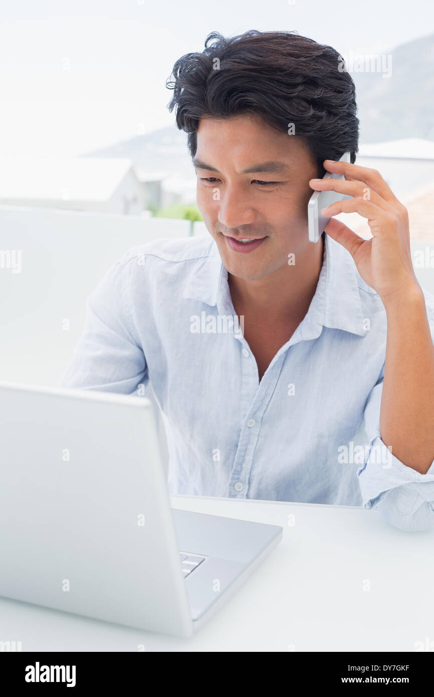 Smiling man using his laptop and talking on phone Stock Photo - Alamy