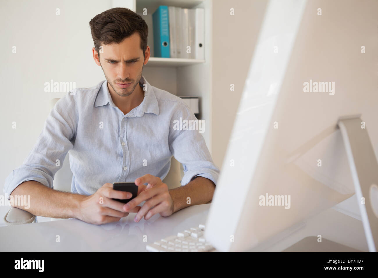 Casual businessman sending a text at his desk Stock Photo - Alamy