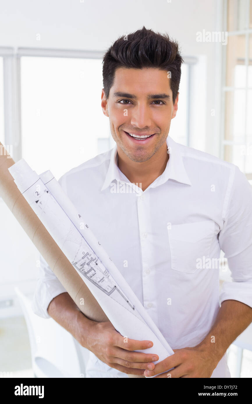 Casual architect smiling at camera holding blueprint in the office ...