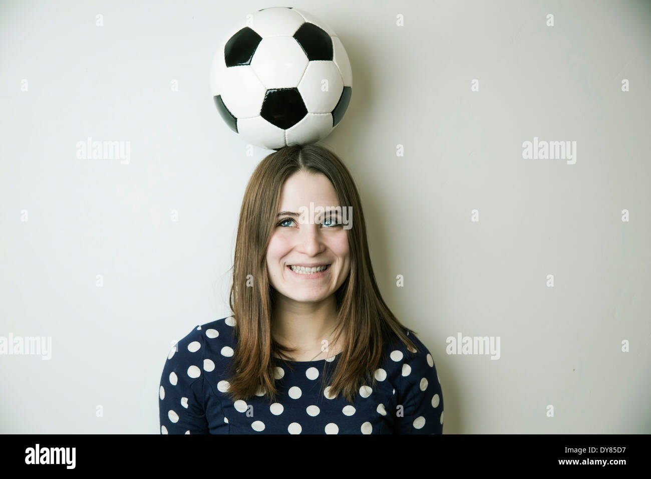 Portrait of smiling teenage girl with football on her head in front of ...