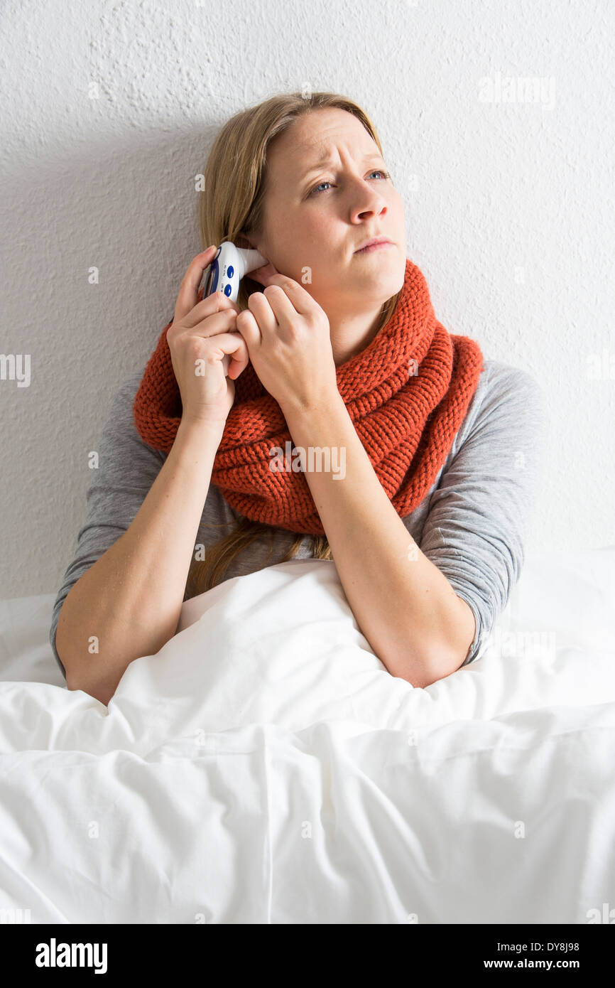 Young woman lying in bed, has a cold, fever, flu, fever, measured with ...