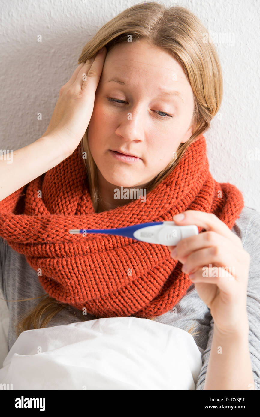 Young woman lying in bed, has a cold, fever, flu, fever, measured with ...