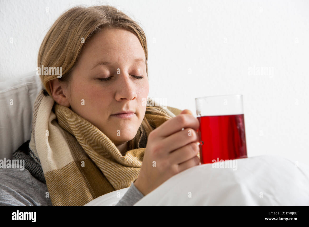Young woman lying in bed, has a cold, drinking a hot tea Stock Photo ...
