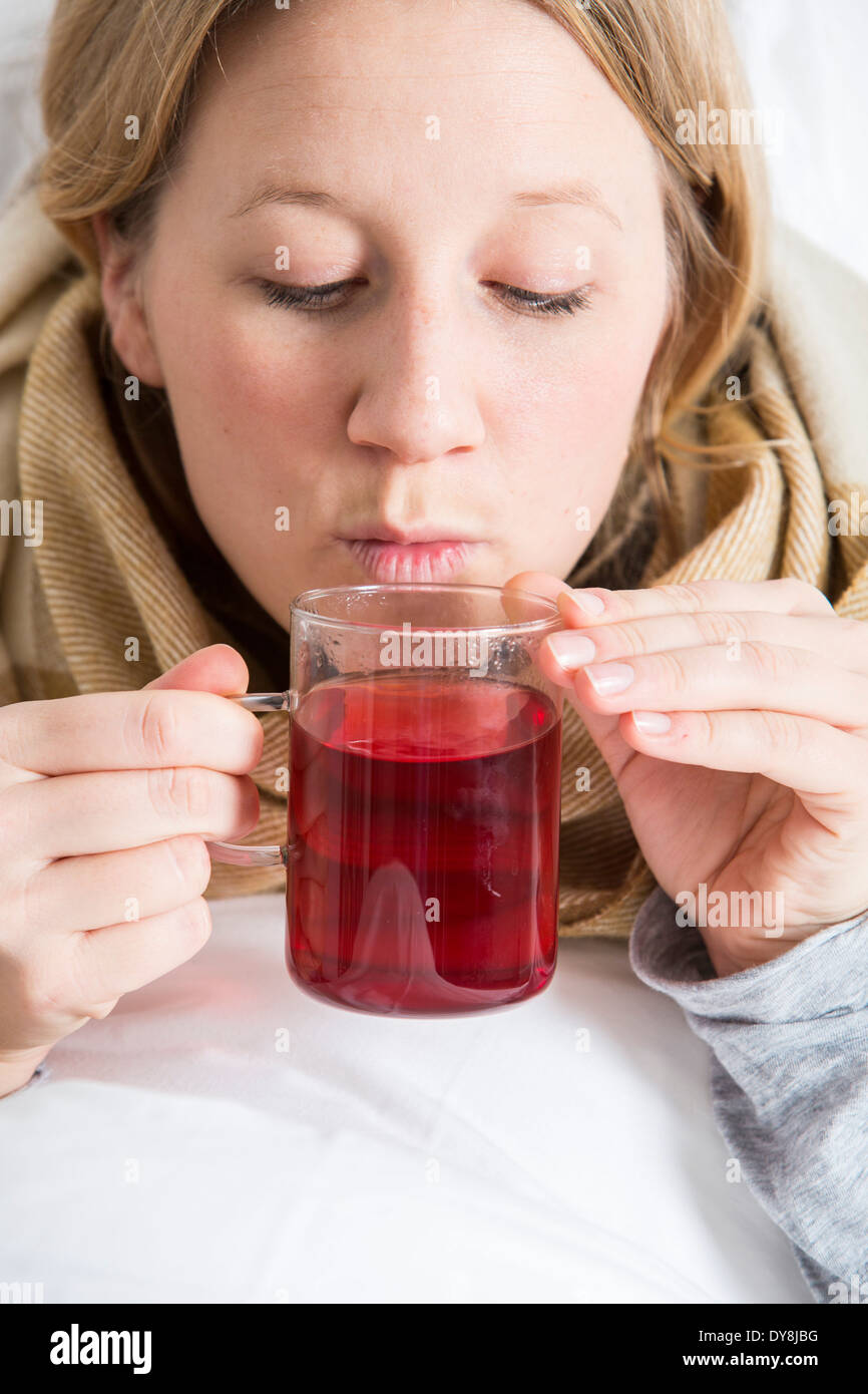 Young woman lying in bed, has a cold, drinking a hot tea Stock Photo ...