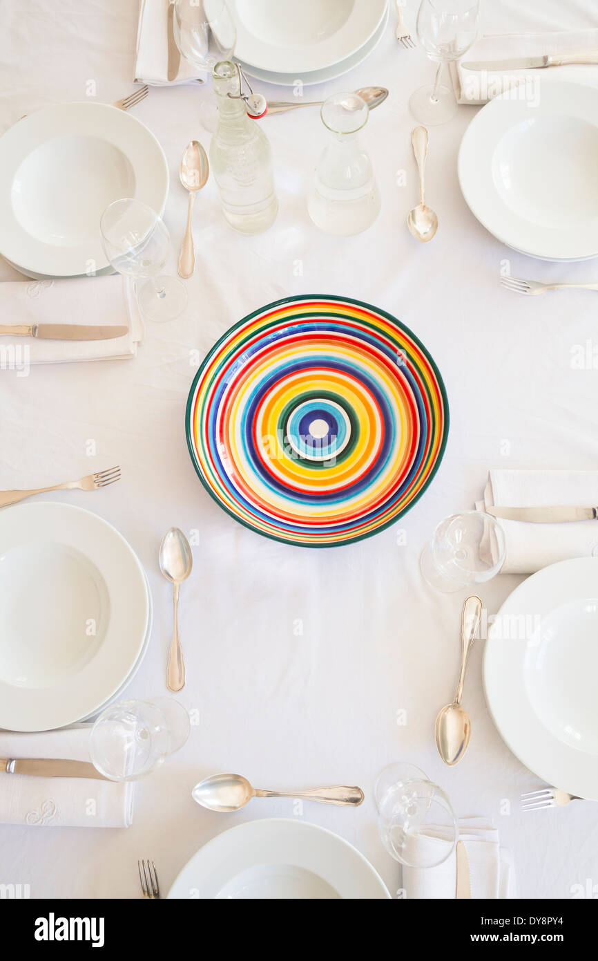 Laid table with six place settings and colourful bowl in the middle of ...