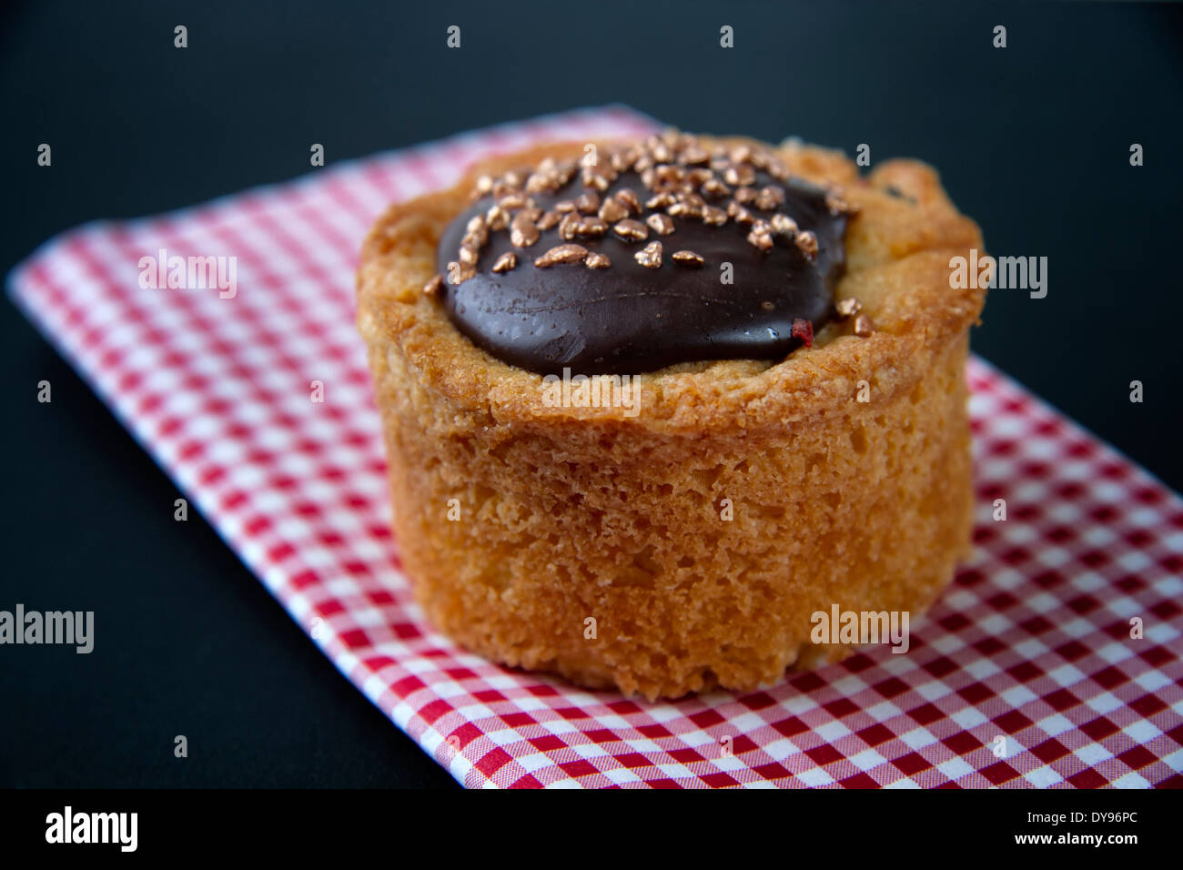 Home baked chocolate iced individual sponge cake on a gingham patterned ...