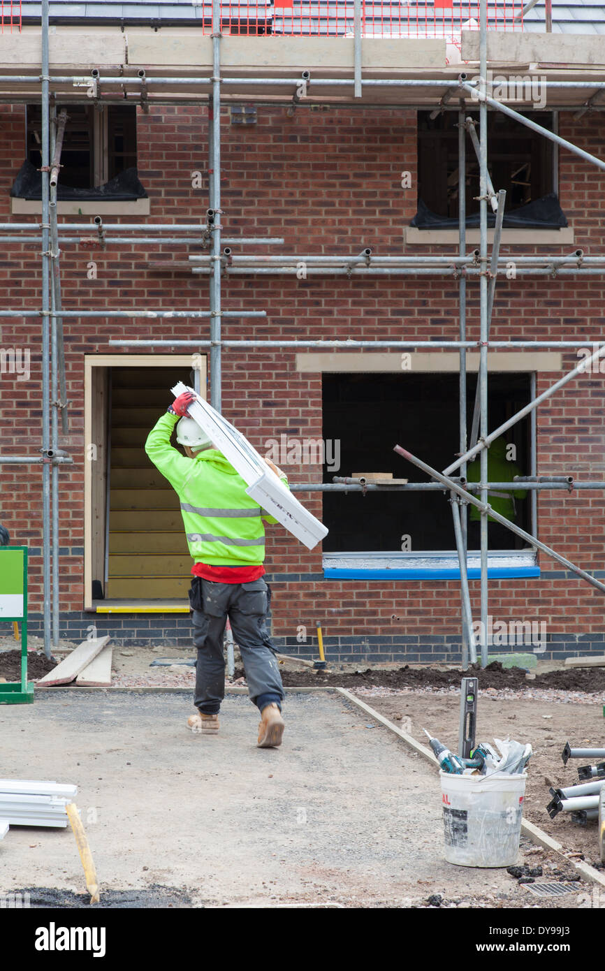 A work man carrying a new PVC window to be installed in a new house ...