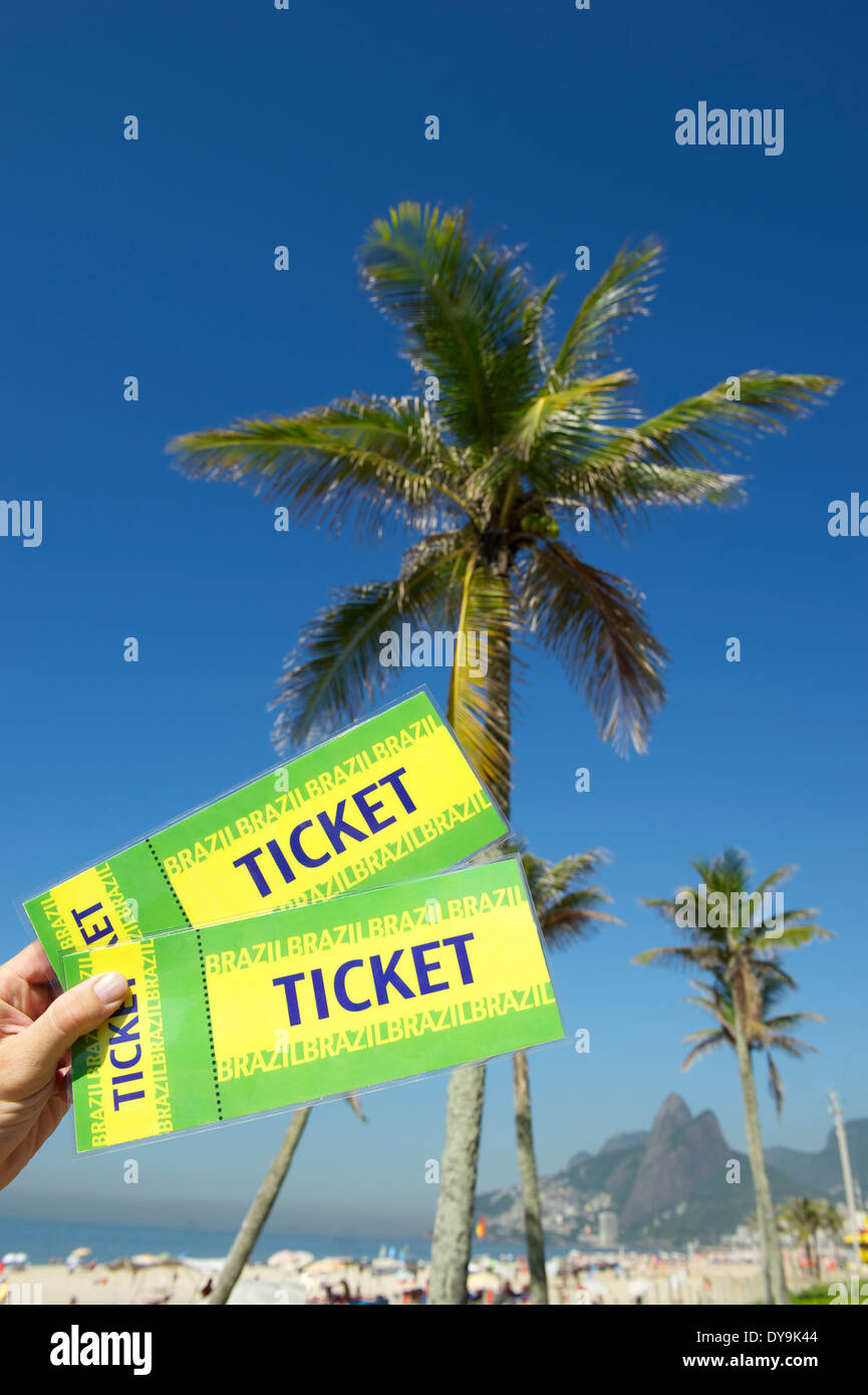 Hand holding pair of Brazil tickets in front of towering palm trees at ...