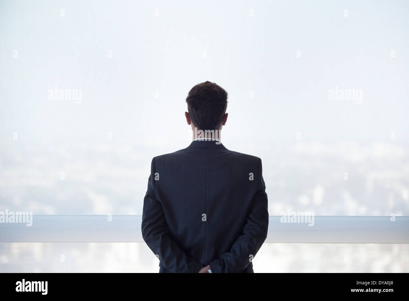 Businessman looking out high rise window at view of city below, rear ...