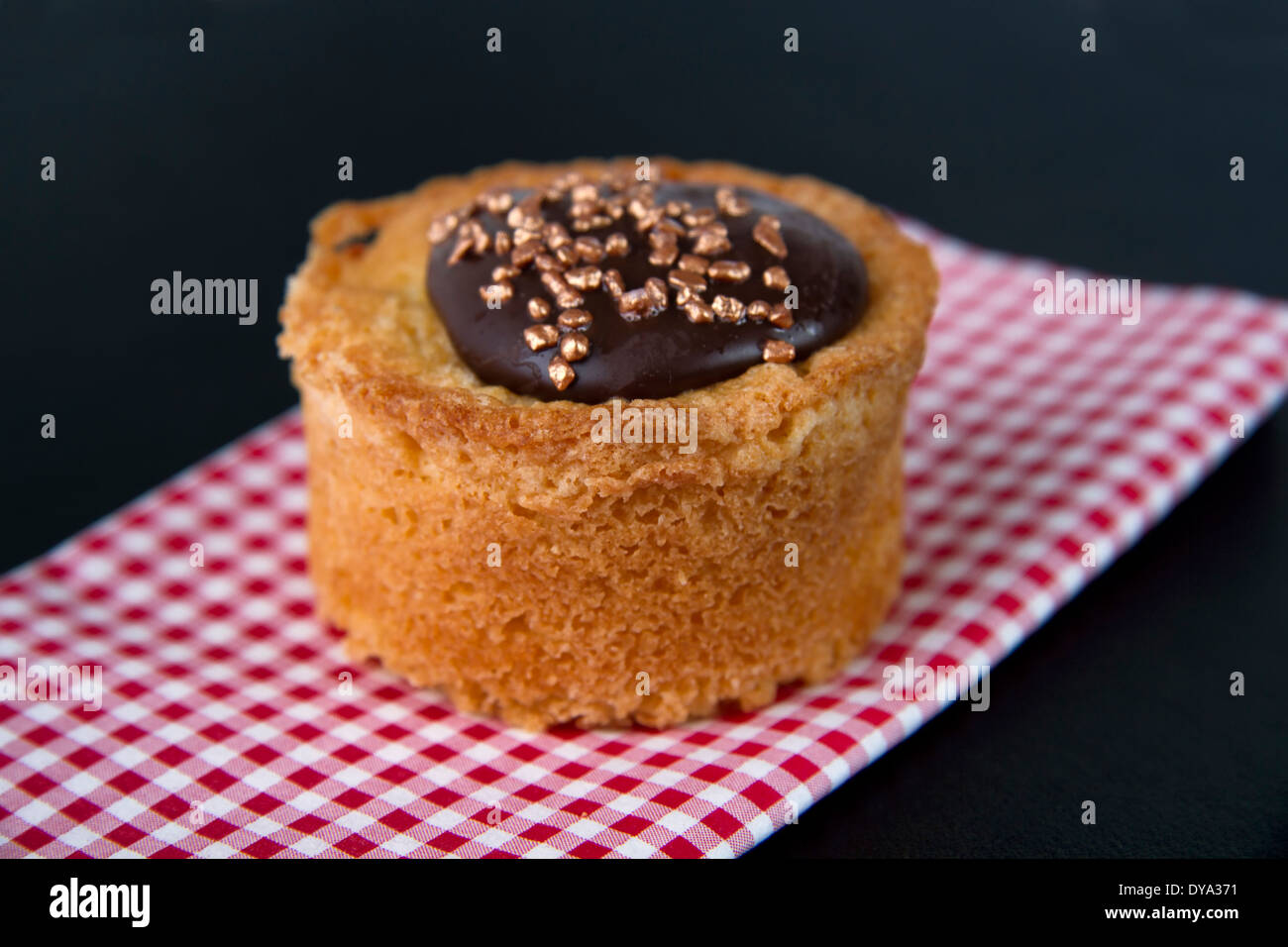 Home baked chocolate iced individual sponge cake on a gingham patterned ...