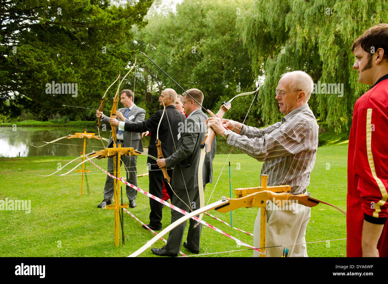 Group of men learning to shoot bows and arrows on green lawn in front ...