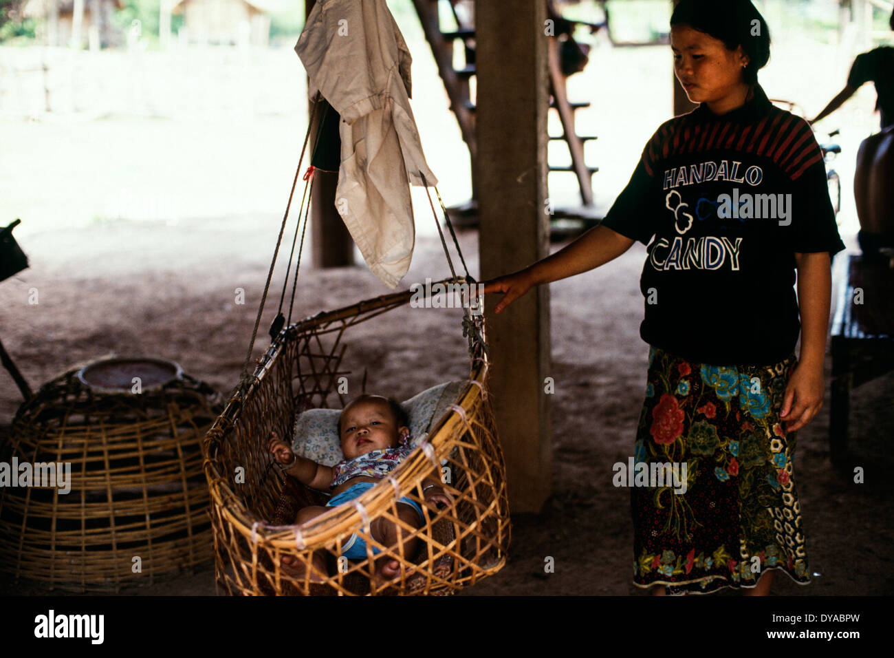 Mother rocks her baby to sleep in a woven crib in the shade of their ...