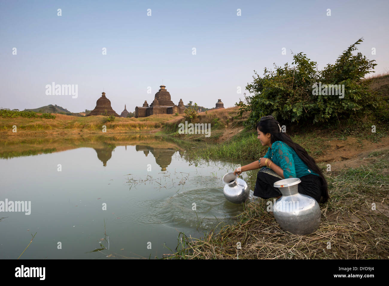 Smiling girl drawing water from a water hole with a vessel made of ...
