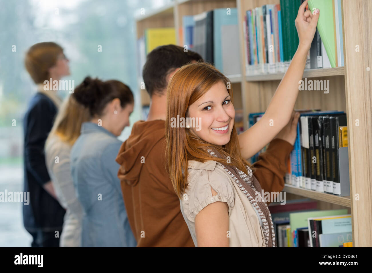 Student choosing book from bookshelf with friend in college library ...