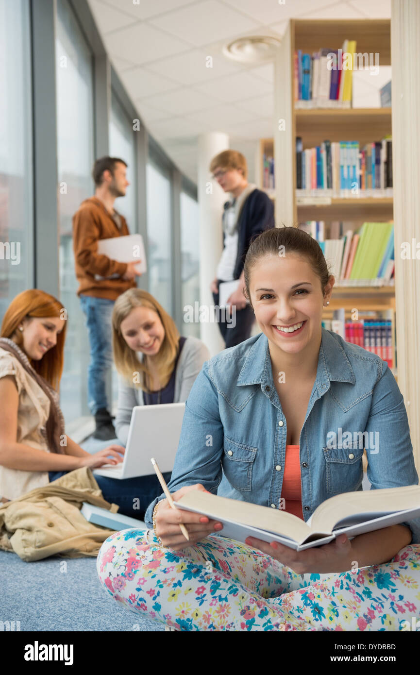 Happy student with classmates in background sitting in school library ...