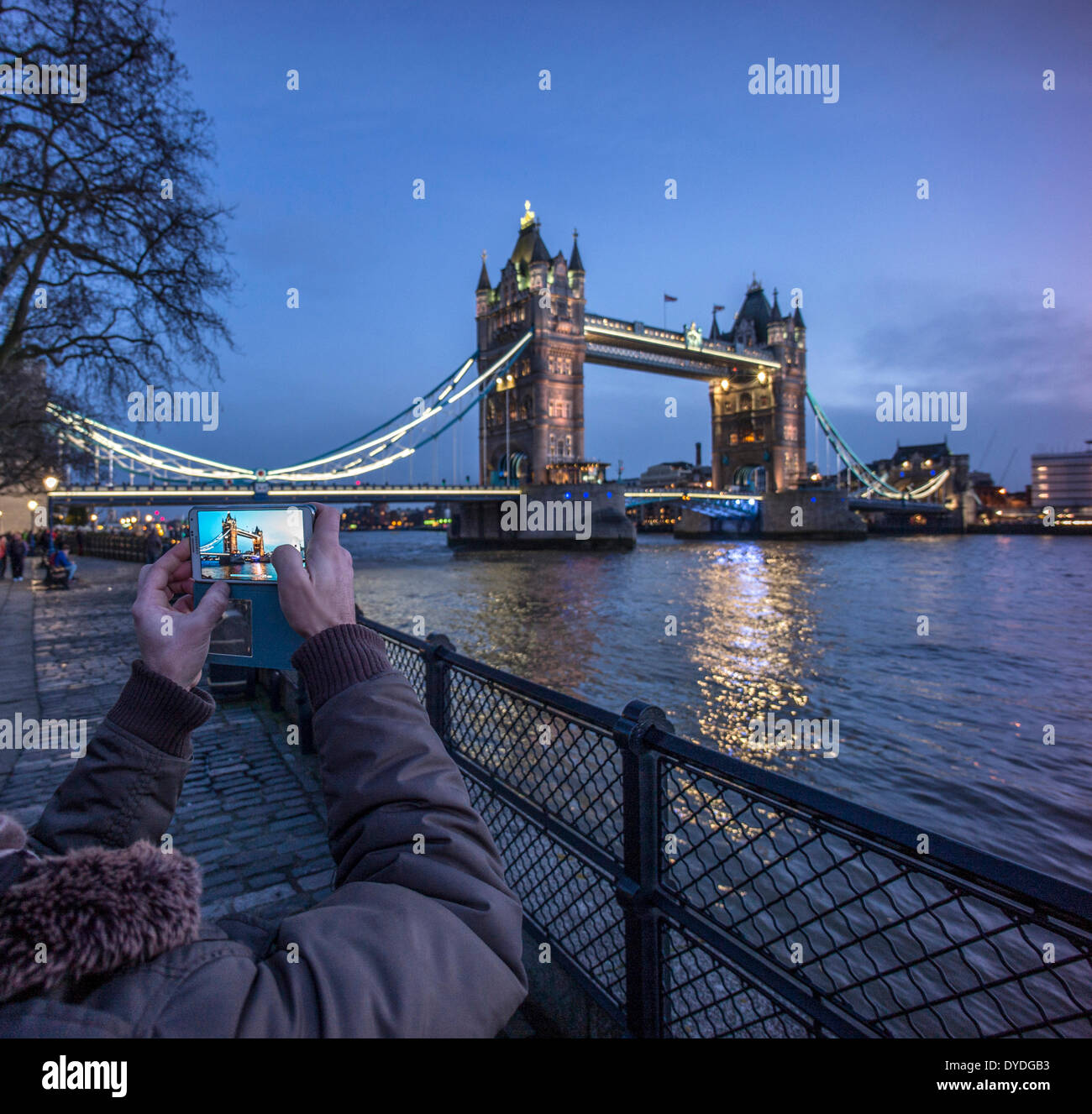 A male tourist takes a picture of Tower Bridge at night from the north ...