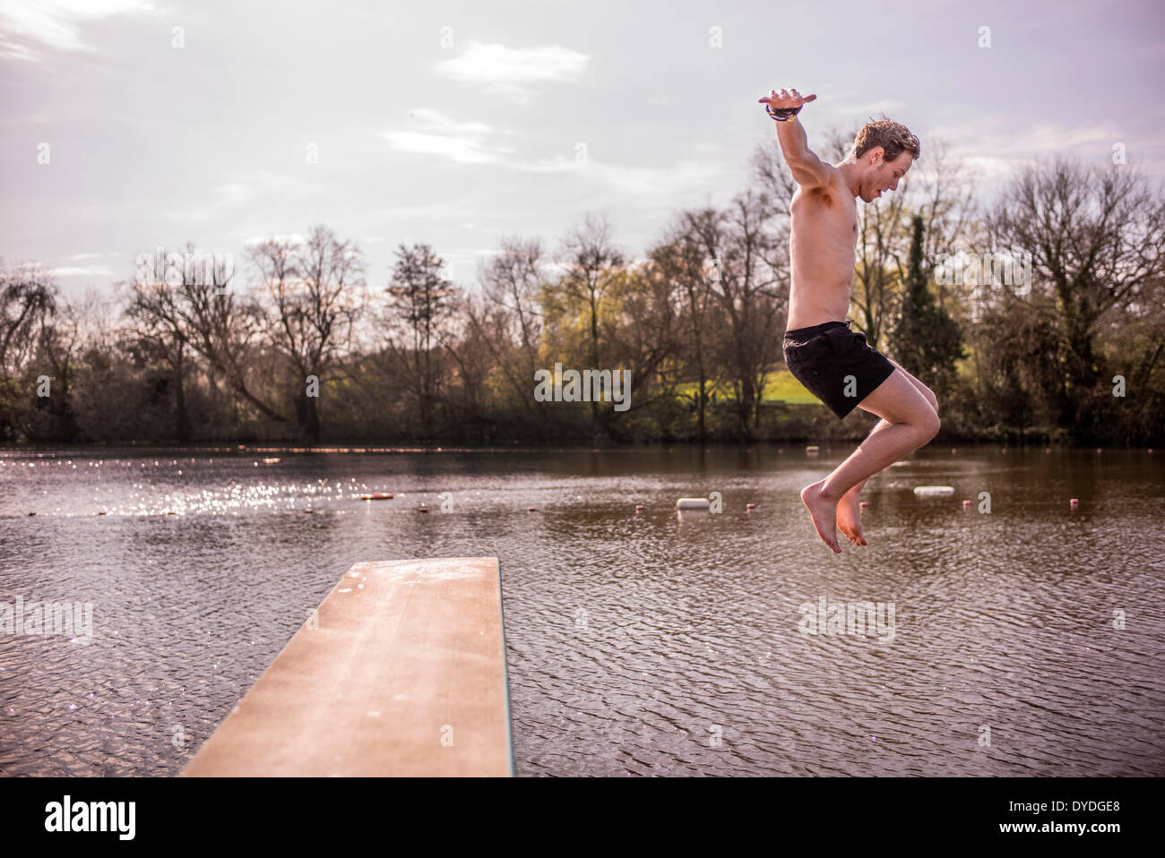 A young man in swimming trunks jumping into spring fresh water ponds ...