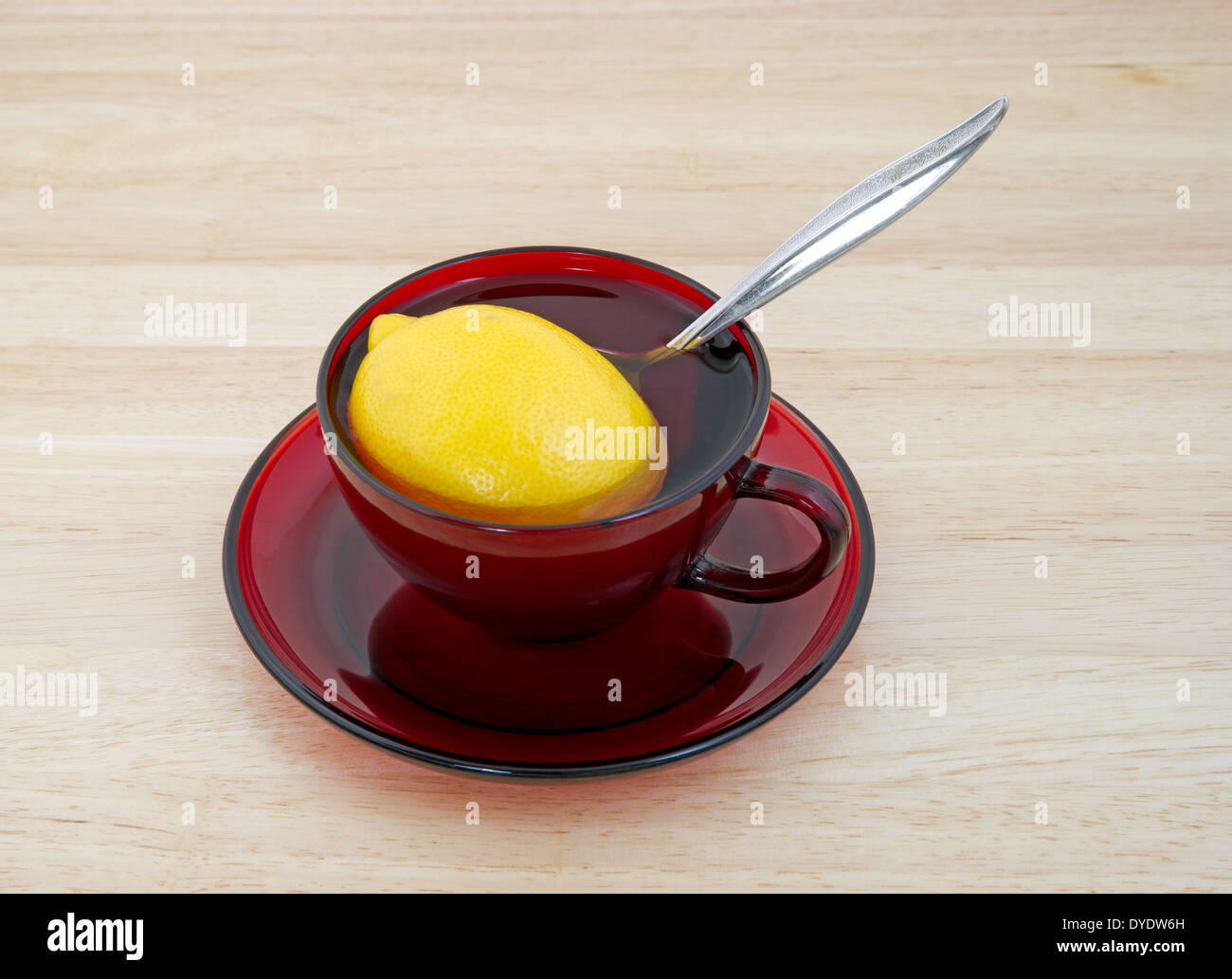 A large lemon in a red cup filled with water and a spoon atop a wood ...