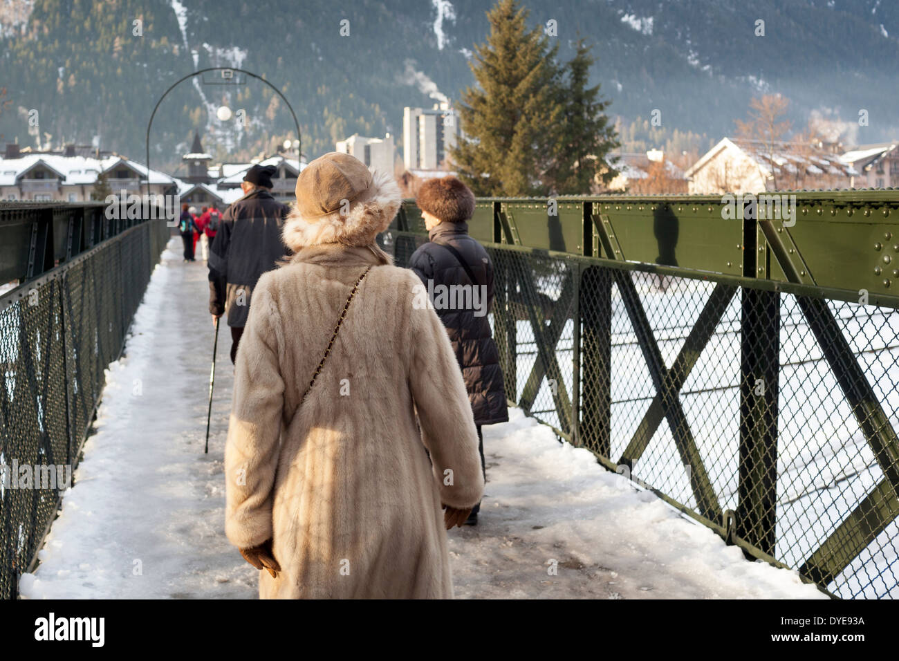 Women wearing fur walk across a pedestrian bridge in the village of ...
