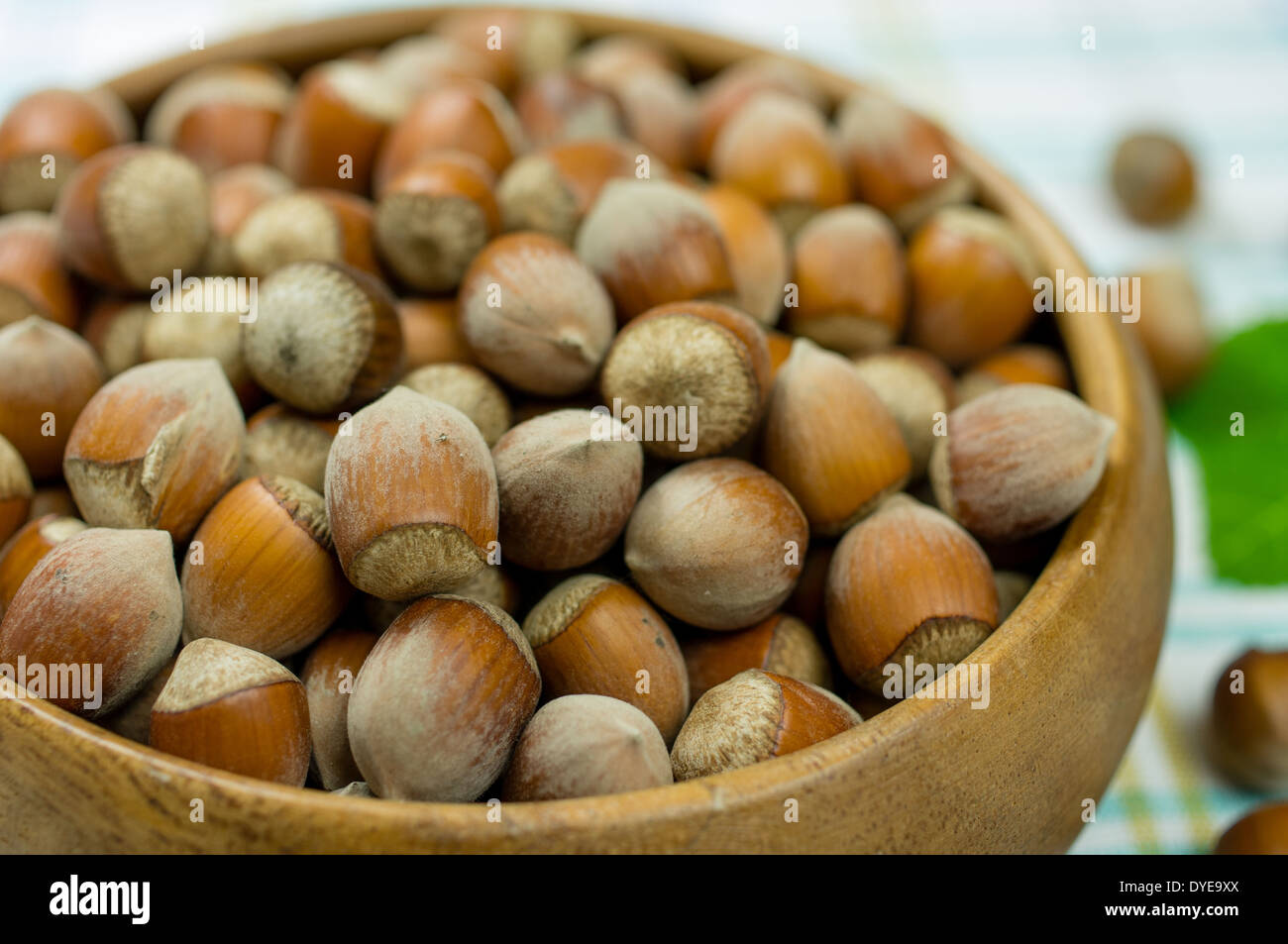 Hazelnuts in a wooden bowl on the table. Random nuts and green leaf ...