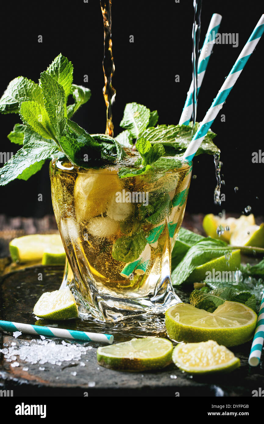 Glass of mojito cocktail with pouring rum and soda, fresh mint, limes ...