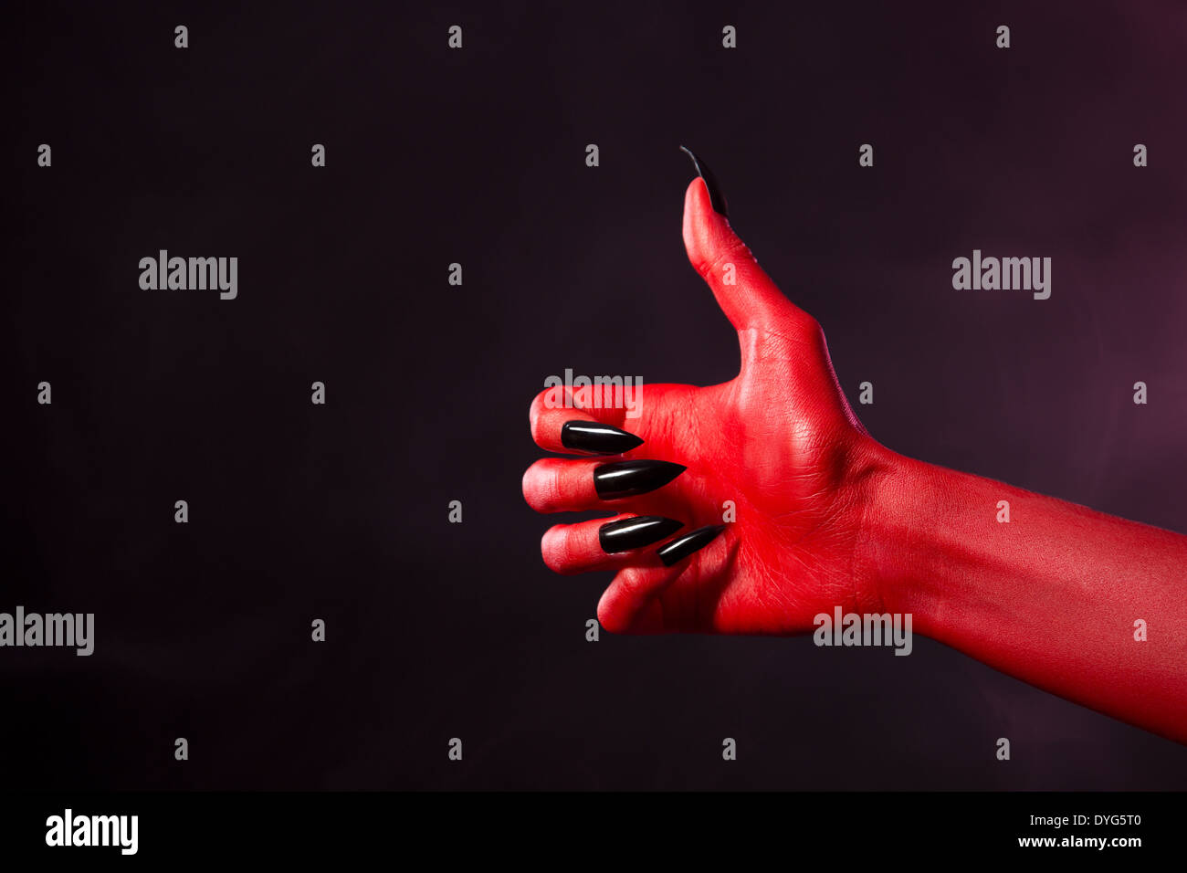 Spooky red devil hand with black nails showing thumbs up, studio shot ...