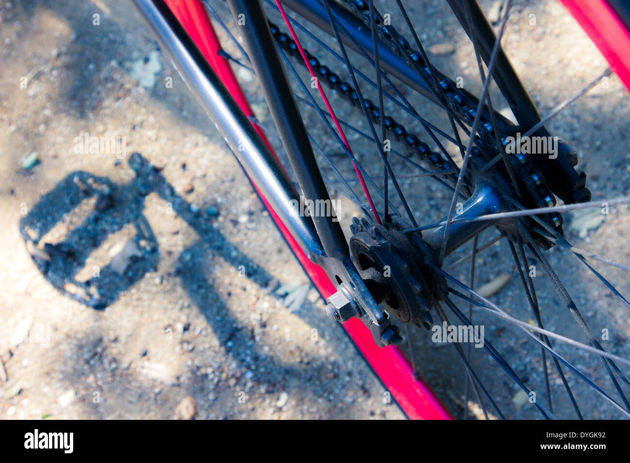 Shadow of bicycle pedal on ground beside bright red bicycle wheel and ...