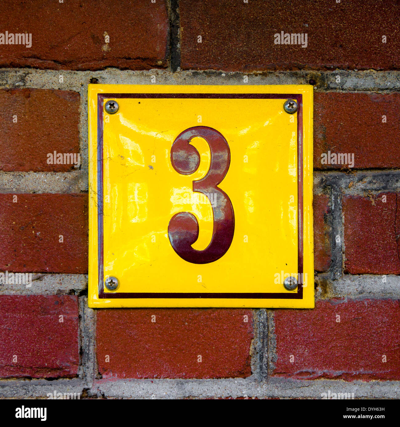 Enameled house number three. Brown lettering on a yellow background ...