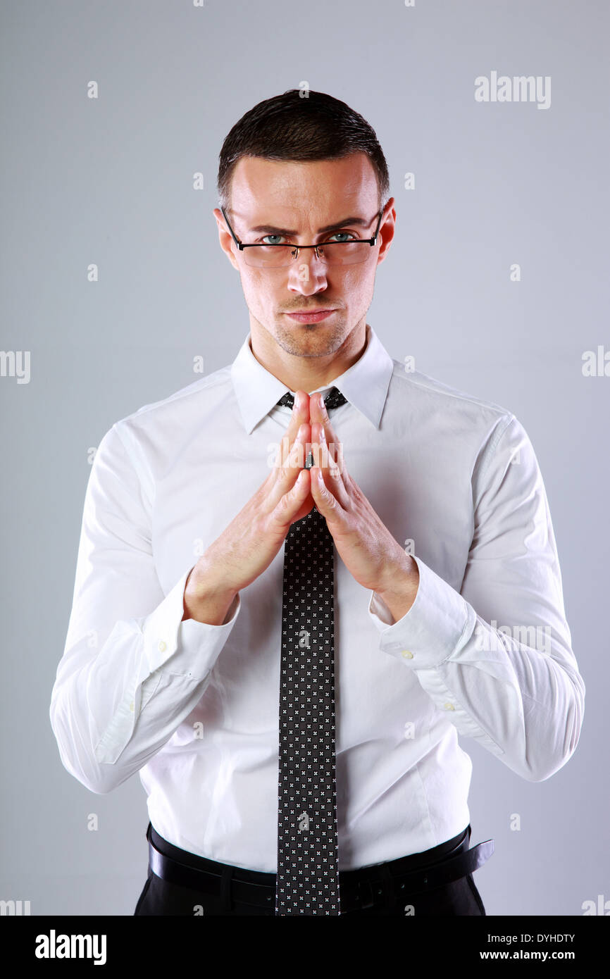 Confident businessman folding his hands together on gray background ...