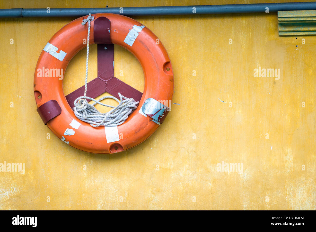 Yellow wall with orange buoy on it. Old lifebuoy with rope inside ...