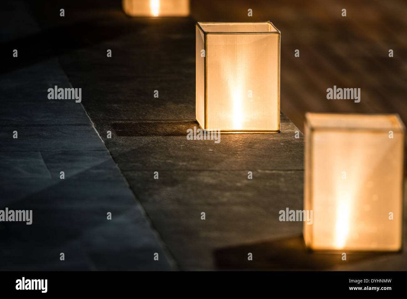 Row of three square lanterns with dim light standing on stone floor ...