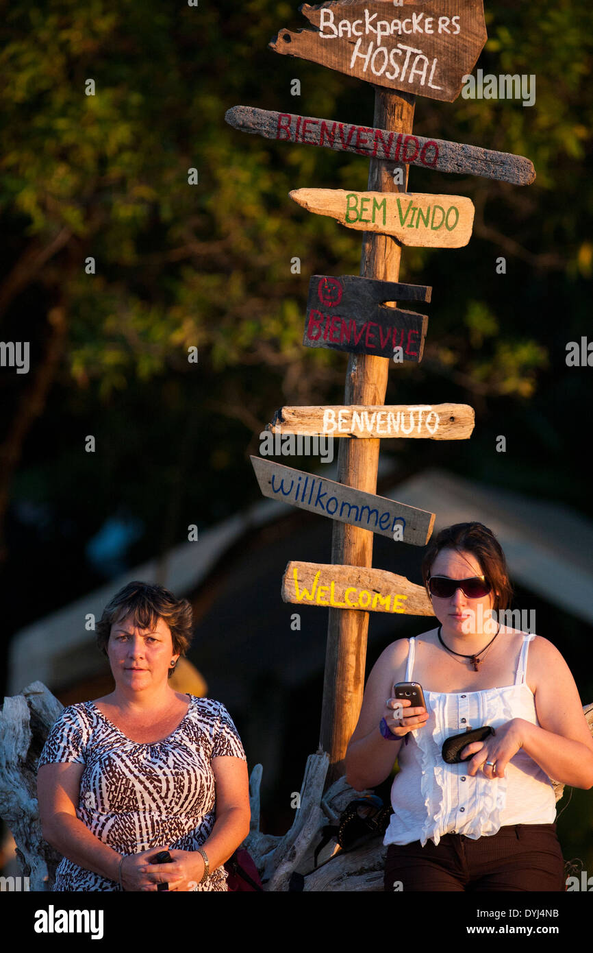 Two tourists stand by a signpost with capital cities on the beach at ...