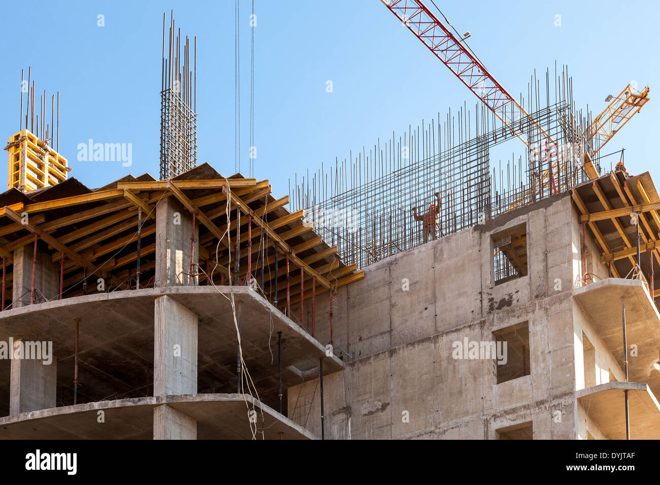 Tall building under construction with crane and worker against a blue ...
