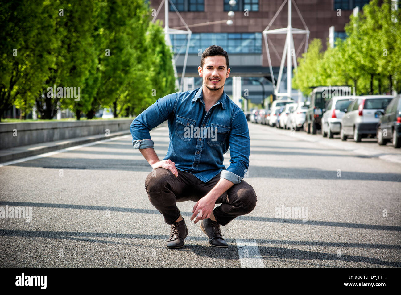 Attractive smiling man sitting in the middle of city road looking at ...