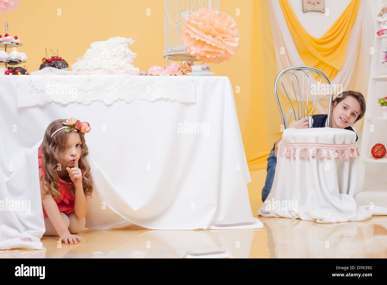 Beautiful girl hiding under table from her brother Stock Photo - Alamy