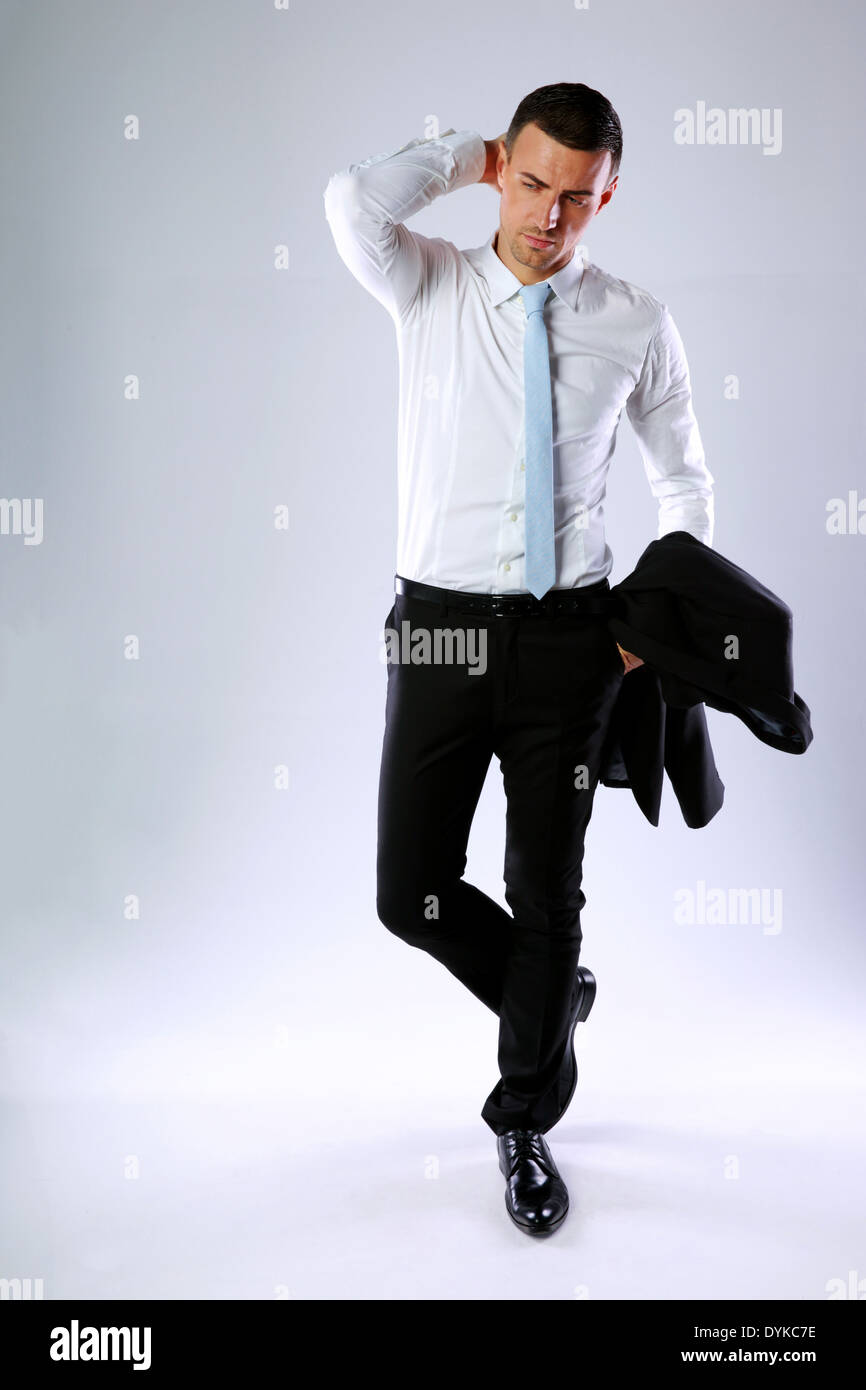 Full length portrait of a pensive business man holding jacket on gray ...