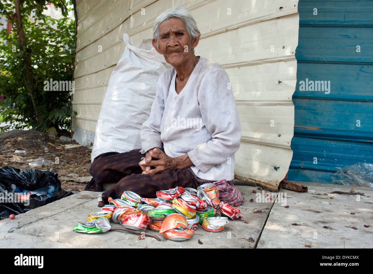 An elderly woman living in poverty is crushing softdrink cans on a city ...