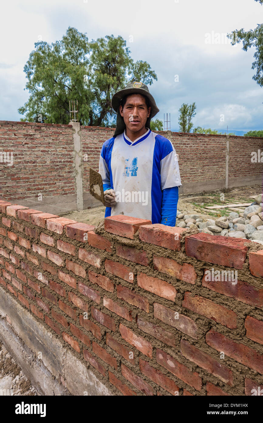 A Bolivian male mason is standing by the brick wall of a house he is ...