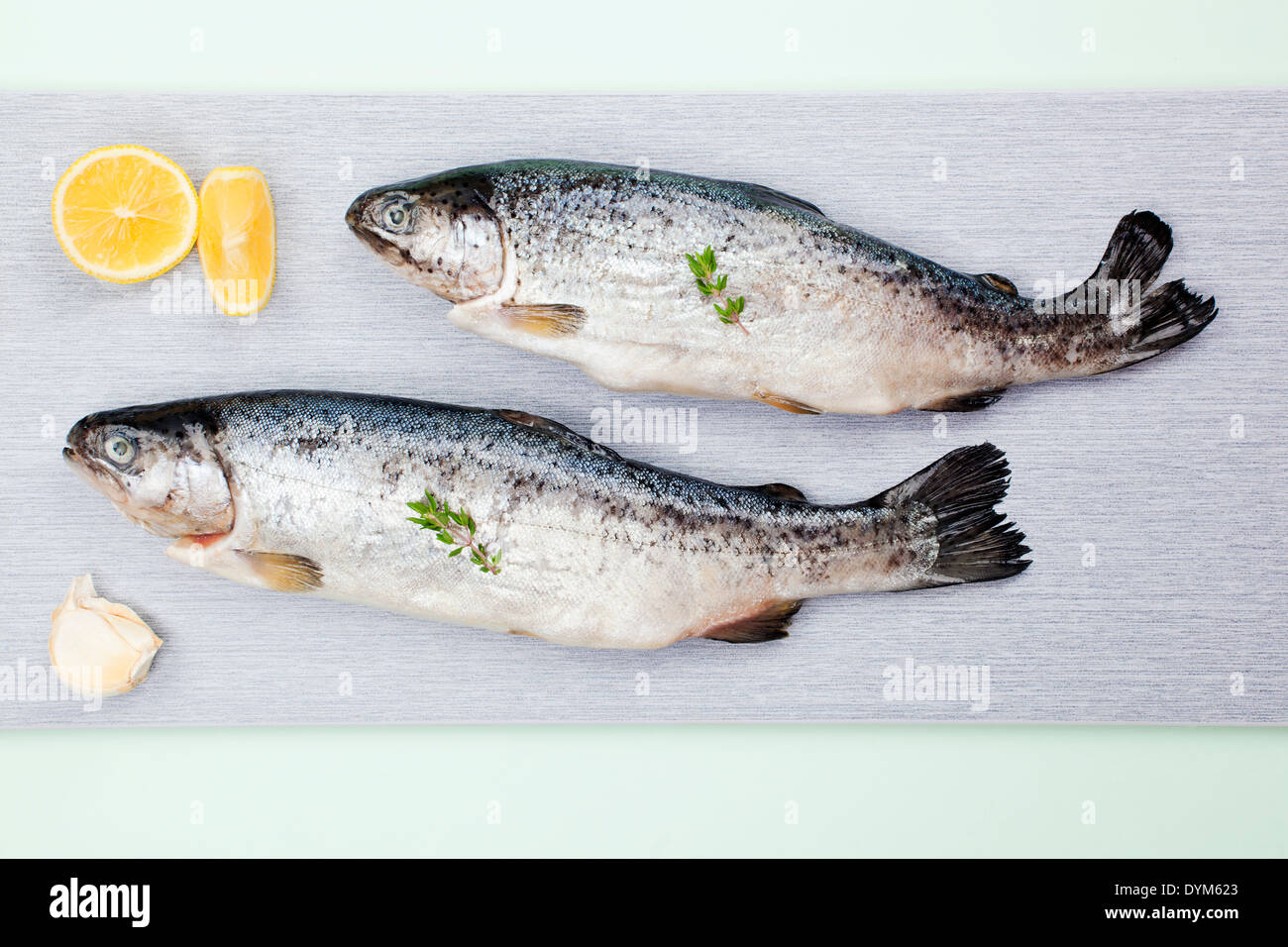 Two fish isolated on board with lemon, garlic and salt corns. Seafood ...