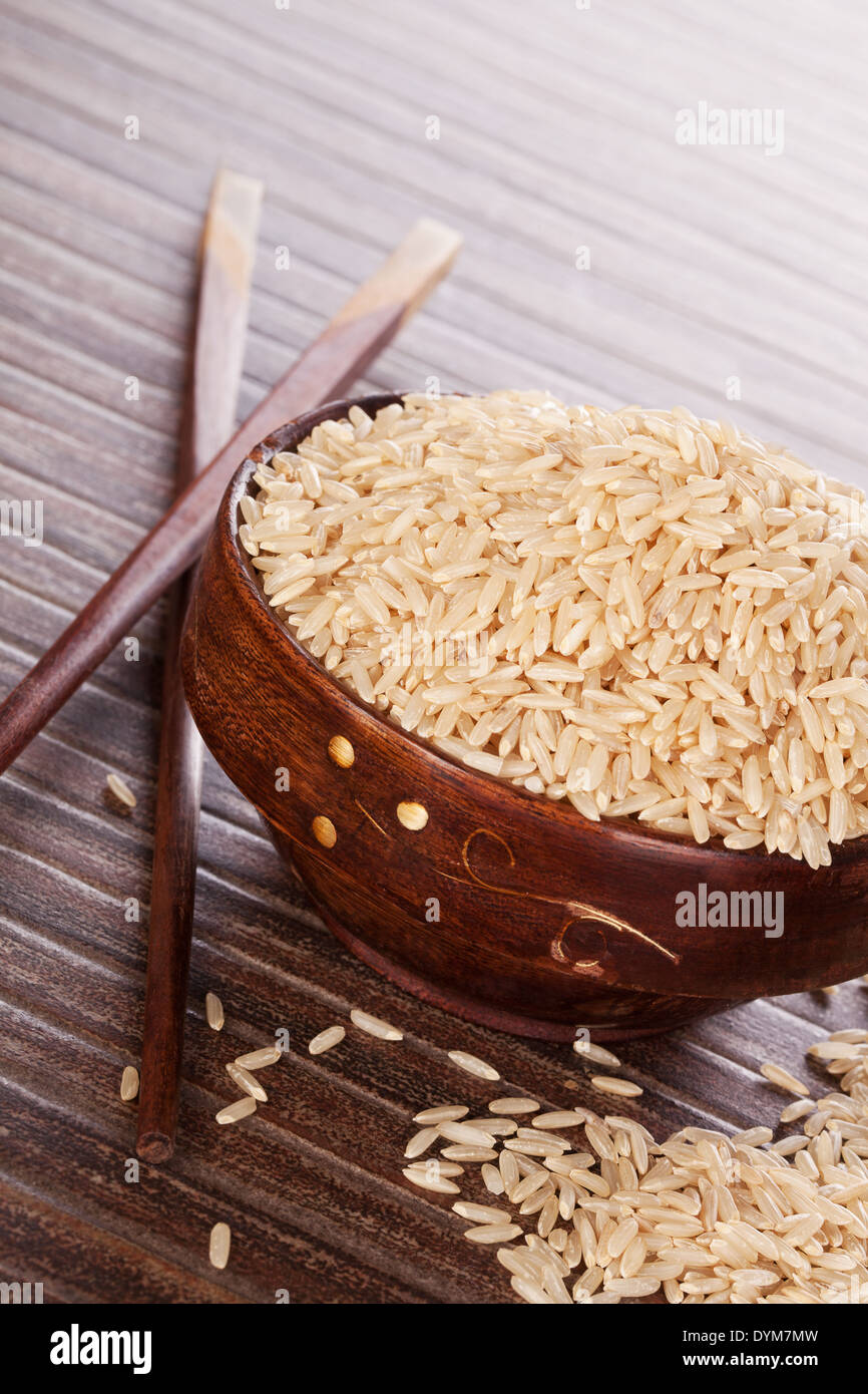 Natural brown rice background. Raw uncooked rice in wooden bowl with ...