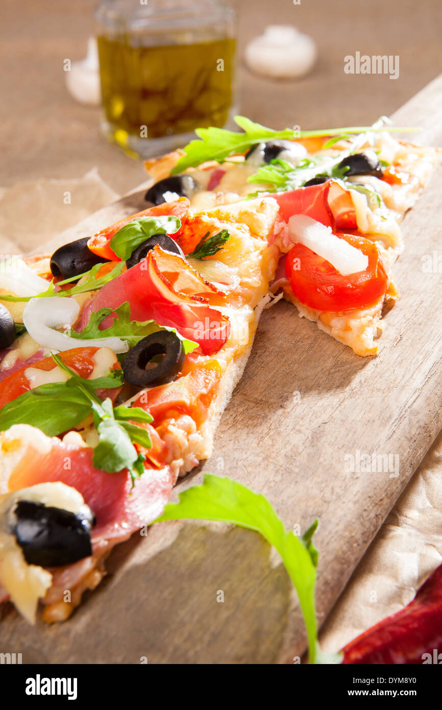 Culinary pizza eating. Pizza with prosciutto, ham, black olives, herbs ...