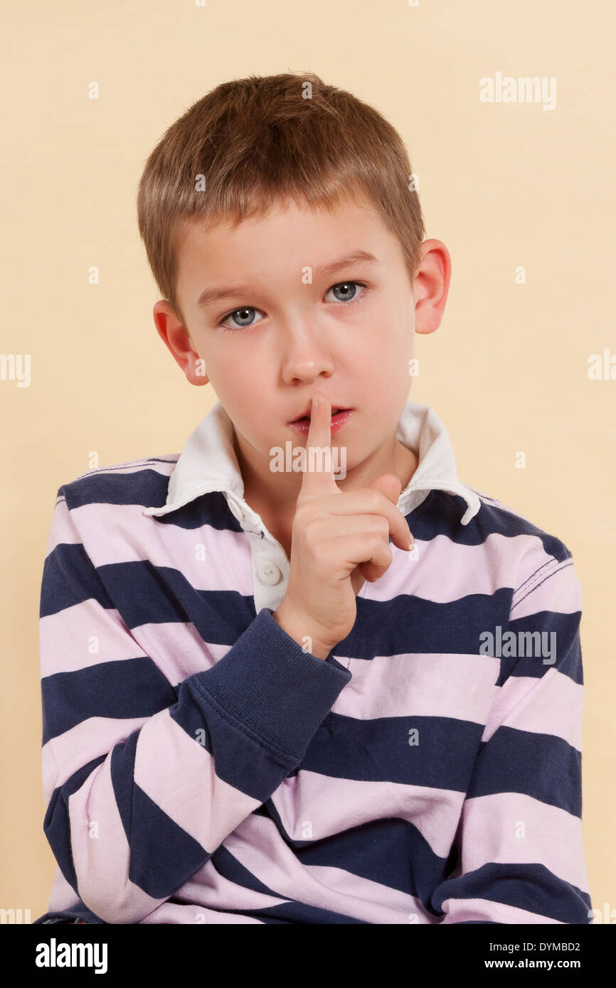 The secret. Don't tell anyone. Young sad boy with finger over his mouth ...
