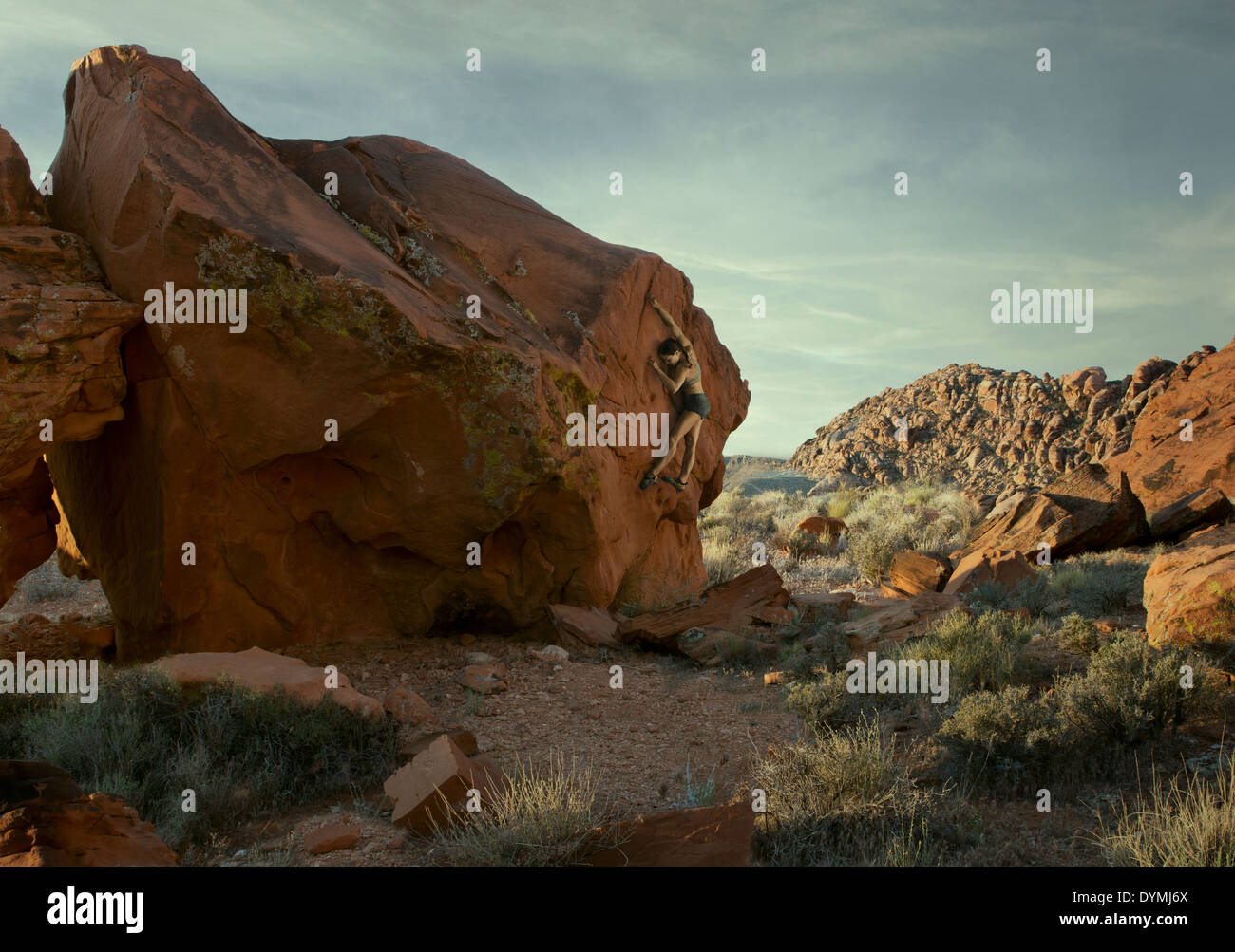 A female climber boulders a golden orange sandstone boulder face in the ...