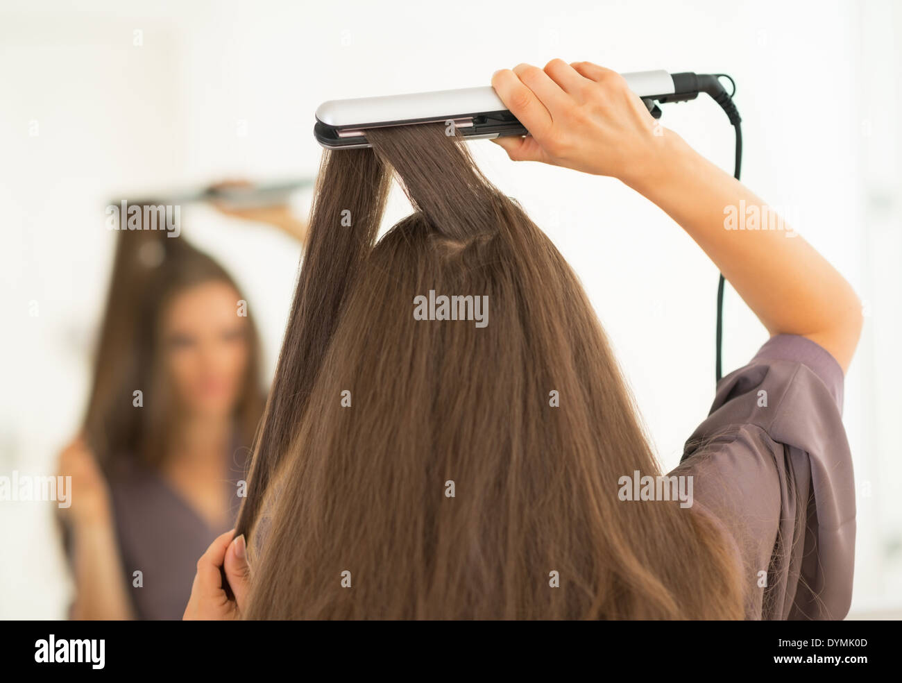 Young woman using hair straightener in bathroom. rear view Stock Photo ...
