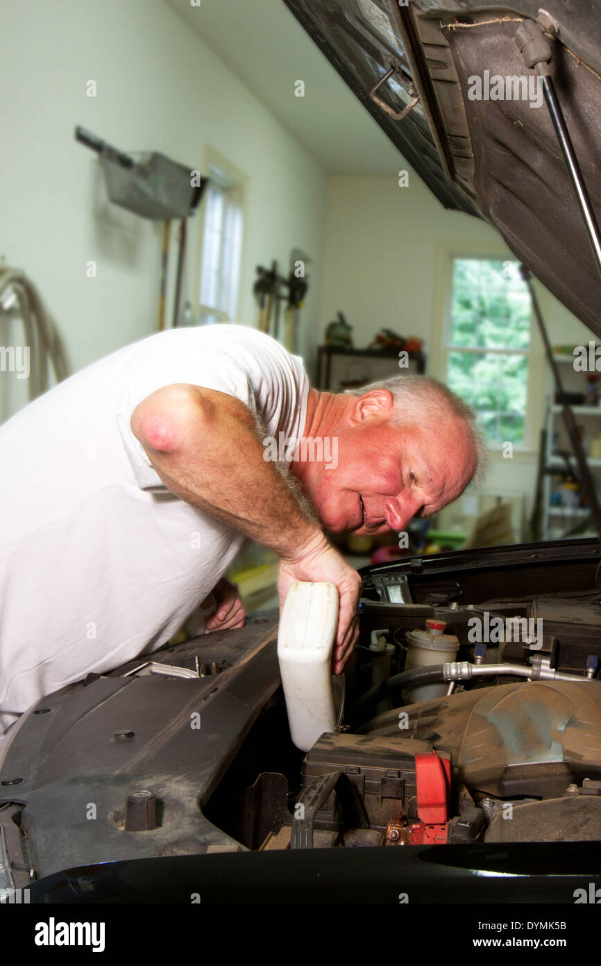Man performing routing maintenance by adding oil on automobile in home ...