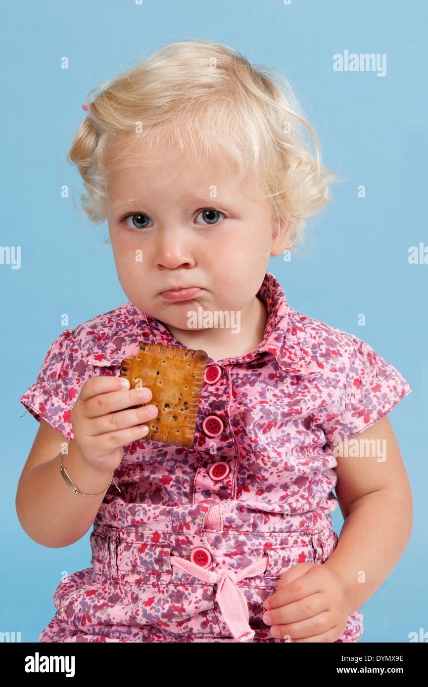 Little girl eating a biscuit. Isolated on blue background Stock Photo ...