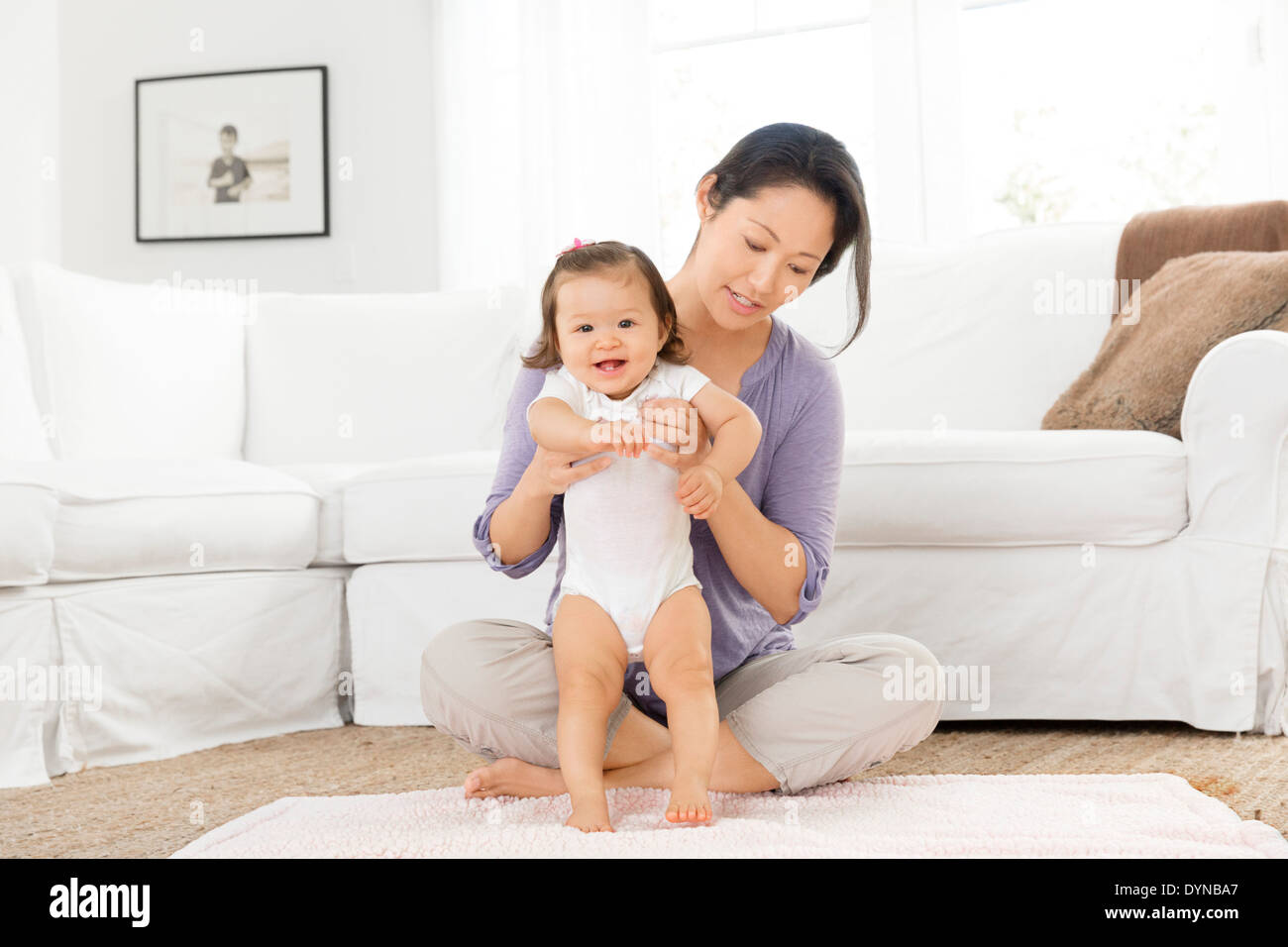 Mother helping baby girl stand in living room Stock Photo - Alamy