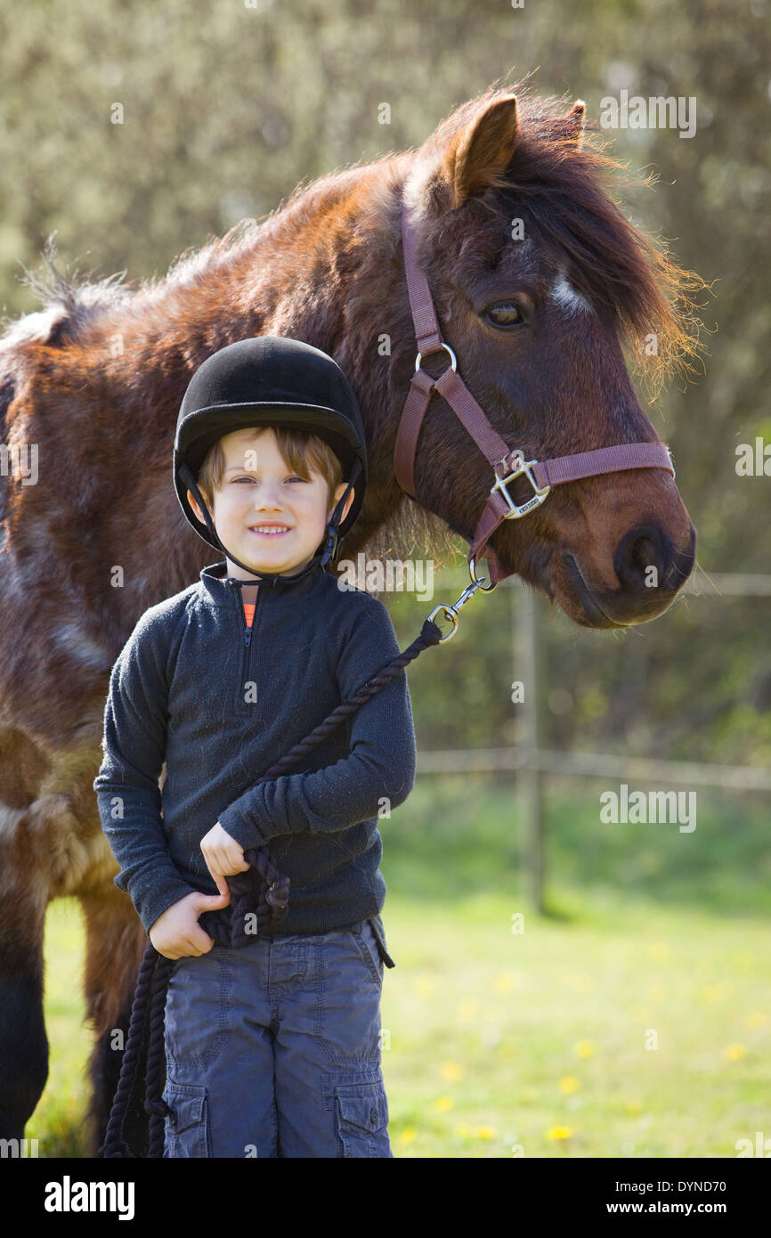 A young boy standing with a pony outside in the countryside on a sunny ...