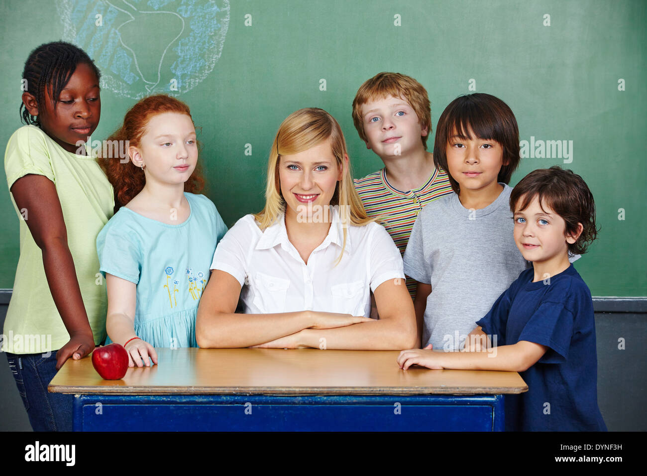 Teacher at desk with elementary school students in front of chalkboard ...