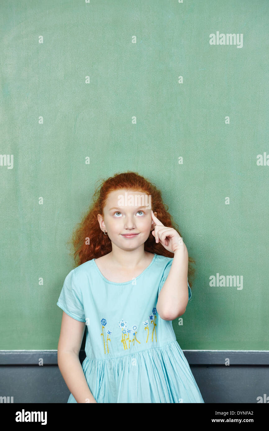 Smart girl thinking in elementary school class in front of chalkboard ...